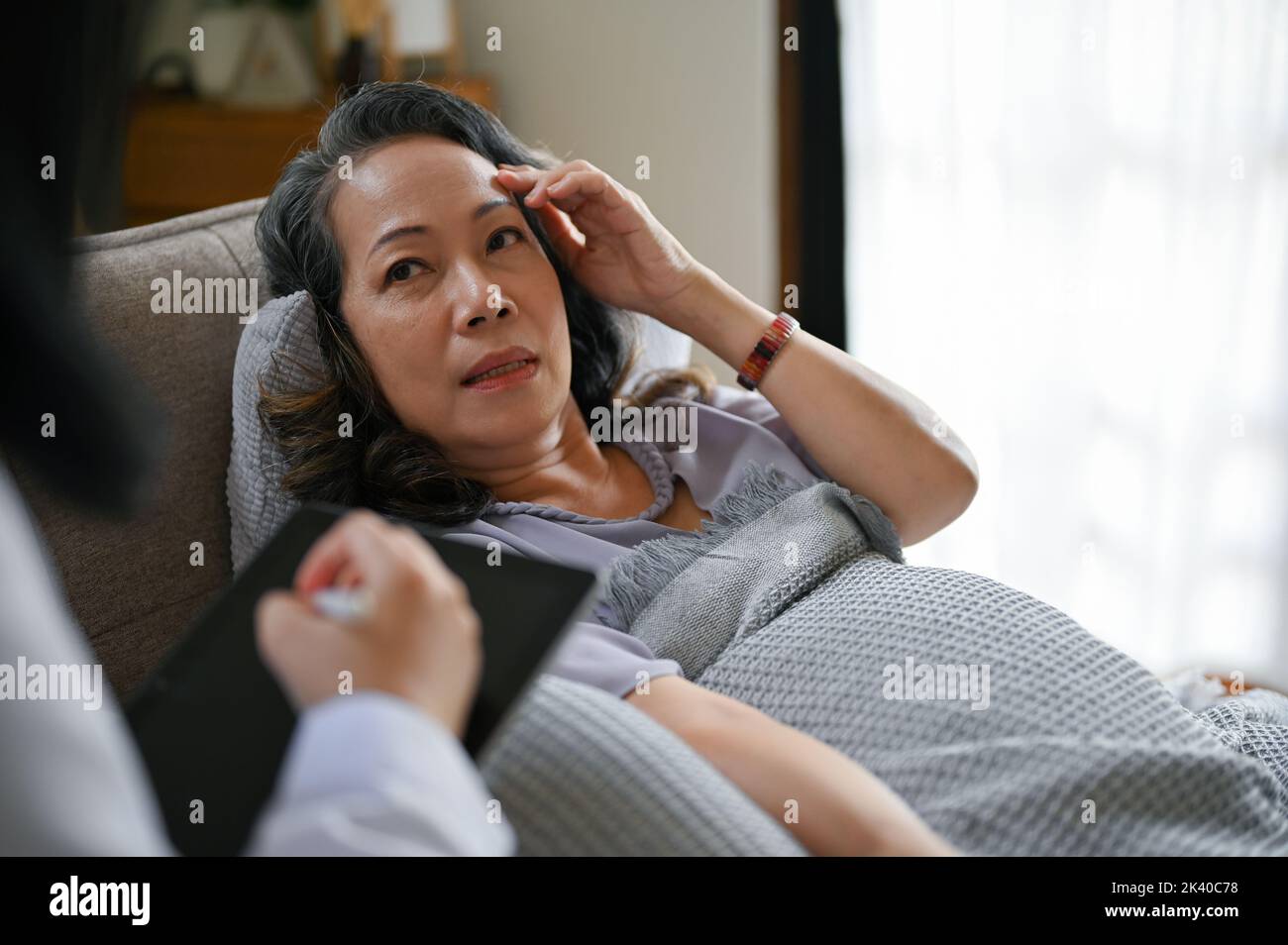 An elderly Asian female patient talking with her doctor in the recovery room. Medical checkup ...