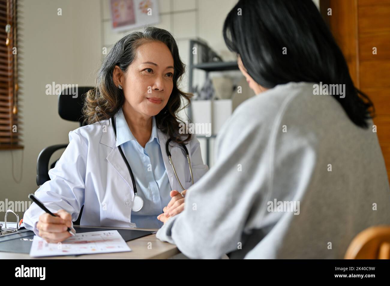 Professional senior Asian female doctor meets with her patient to ...