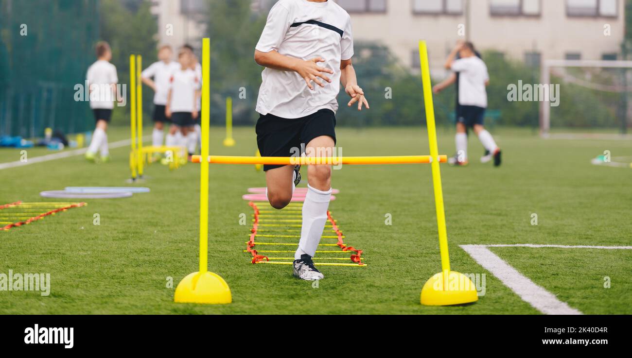 Young boy jumping over ladder and pole at a soccer training session ...