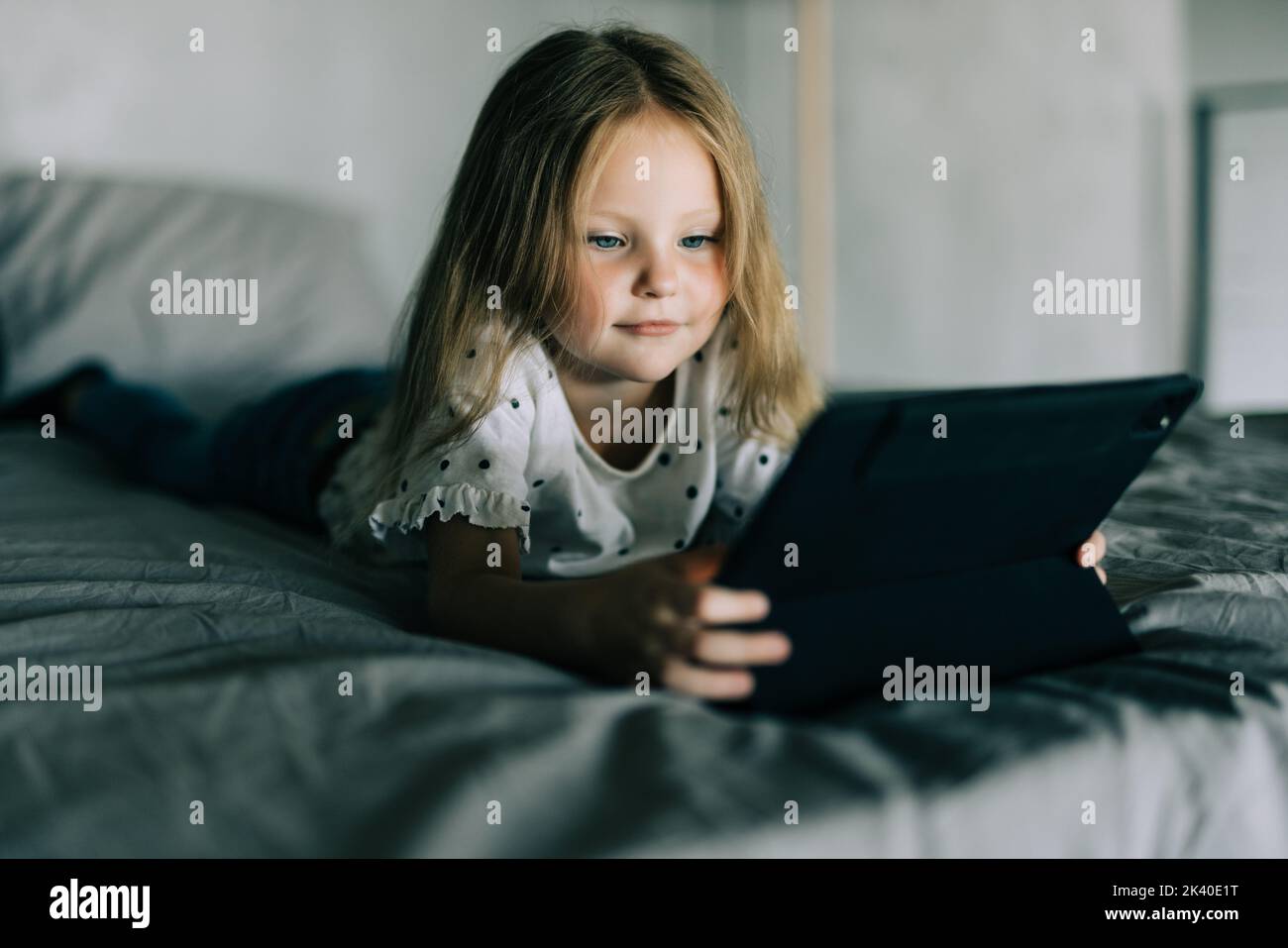 Cute little girl using digital tablet while lying in bed Stock Photo ...