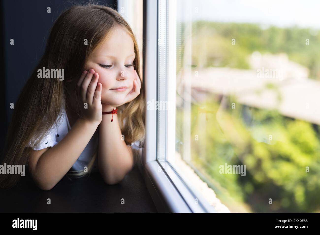 Beautiful little girl smiling and watching out the window. A child ...