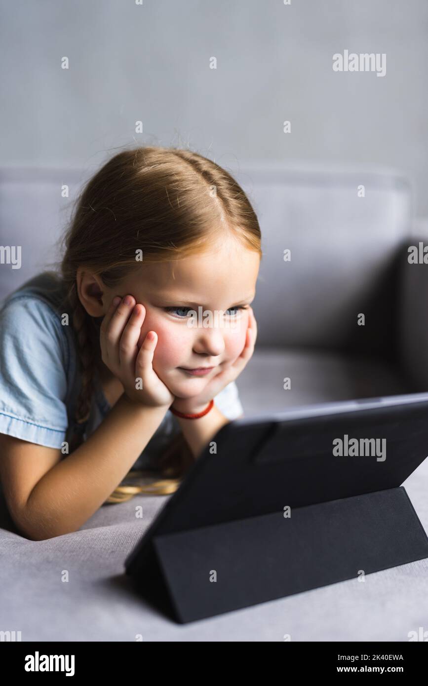 Focused cute preschooler girl watching movie, animated films, cartoons on tablet. Child girl ...
