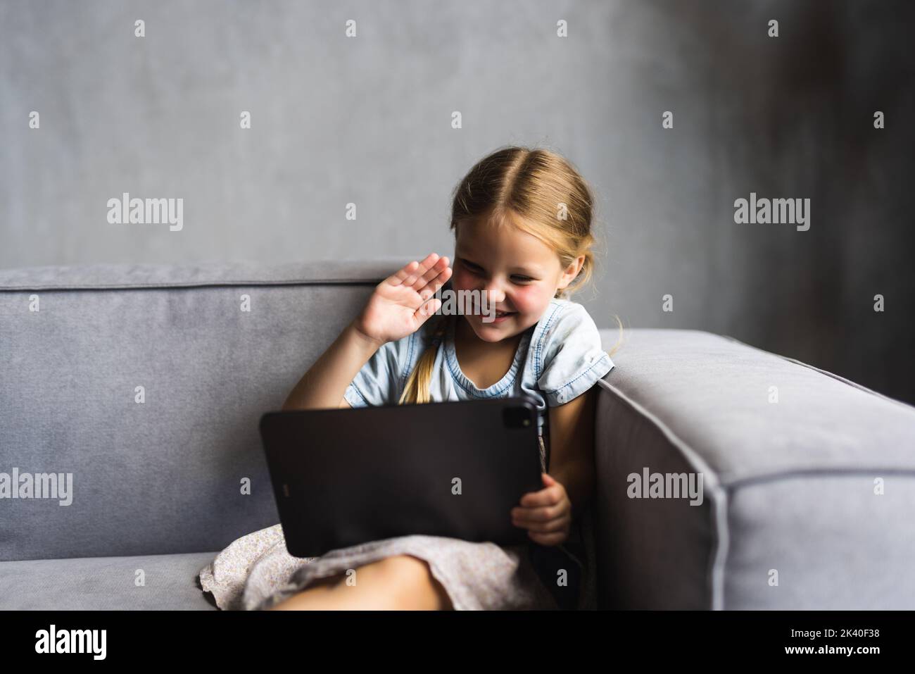 Smiling small Caucasian girl relax on sofa in living room look at pad ...