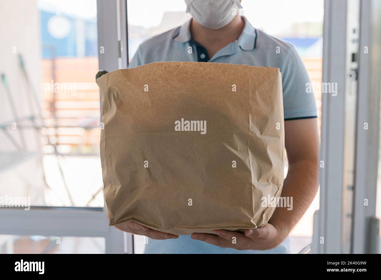 Deliver man wearing face mask in blue uniform handling bag of food give ...