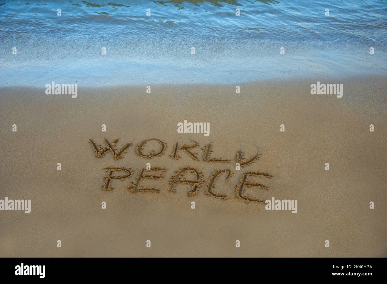 World peace written in the sand on the beach with the sea washing up ...