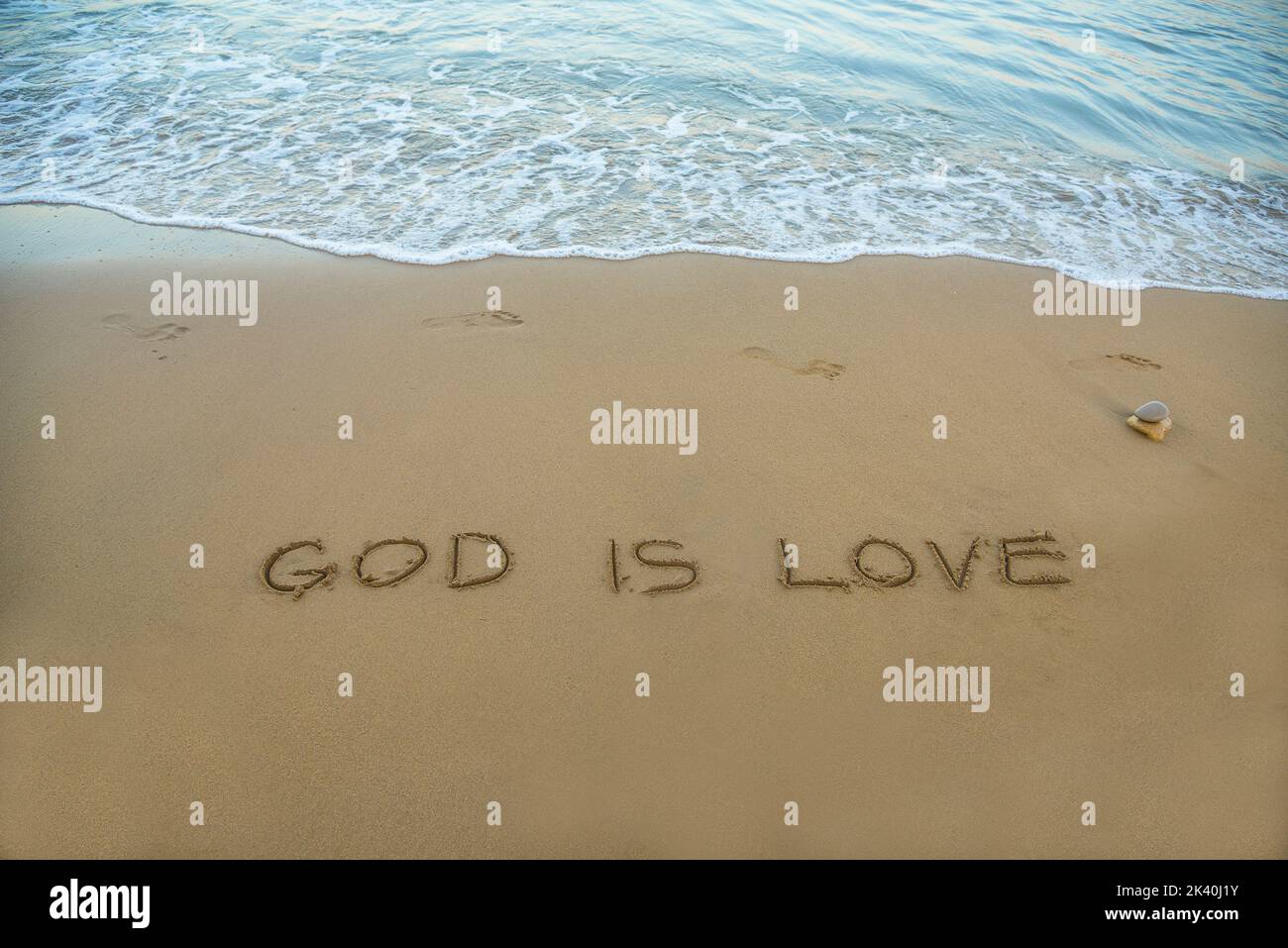 God is love written in the sand on the beach with the sea washing up ...