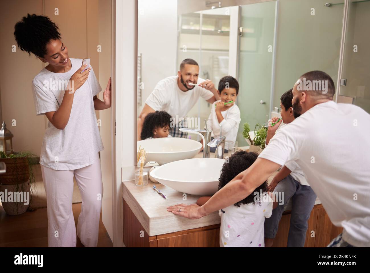 Kids and dad brushing teeth in bathroom, reflection in mirror and mom ...
