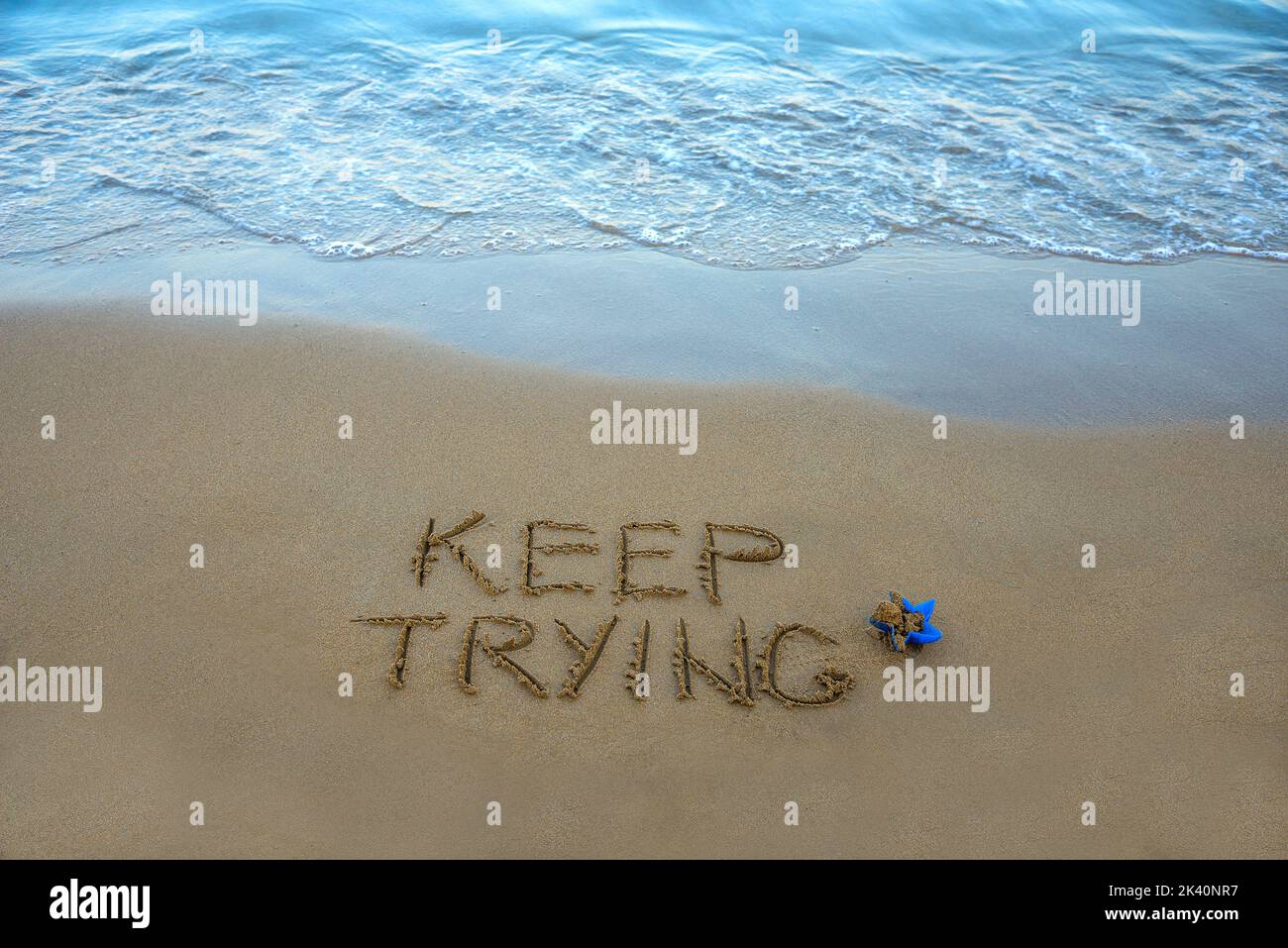 Keep trying written in the sand on the beach with the sea washing up ...