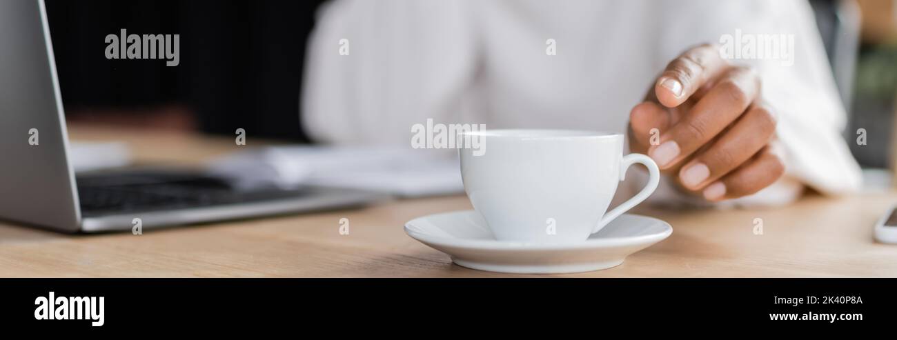 Cropped view of blurred african american businesswoman taking cup near ...