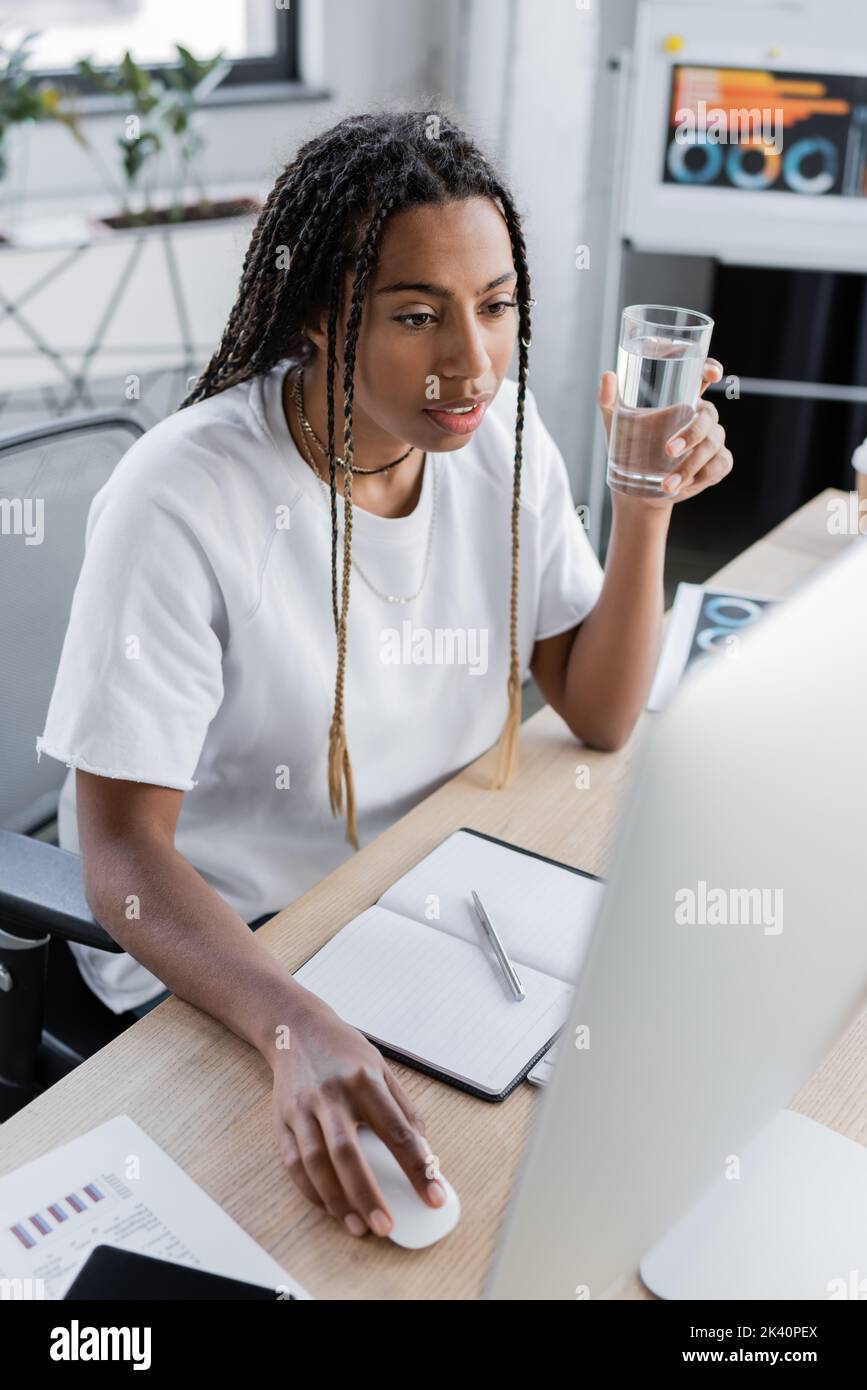 African american businesswoman holding glass of water and using ...