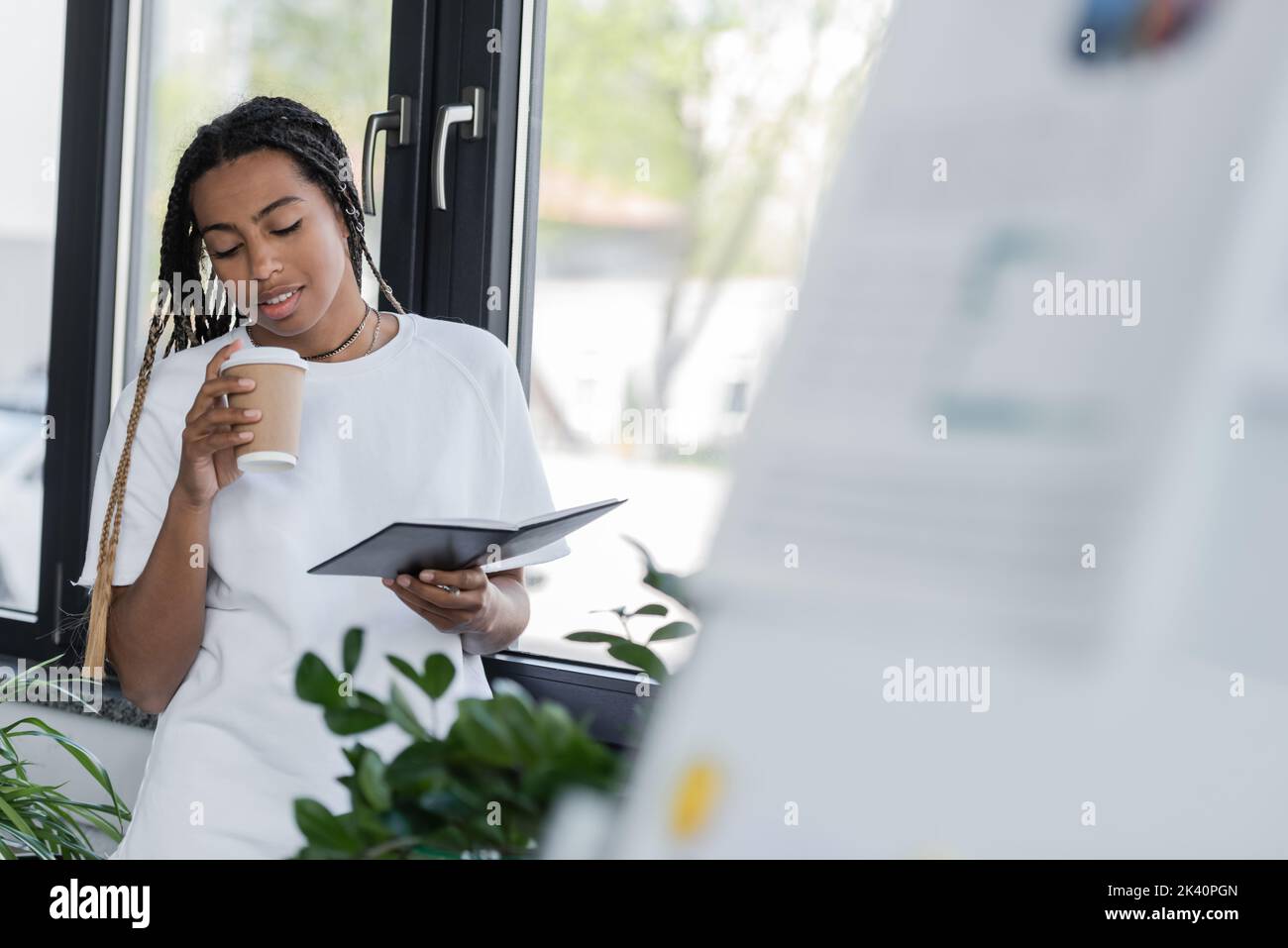 Smiling african american businesswoman holding paper cup and notebook ...