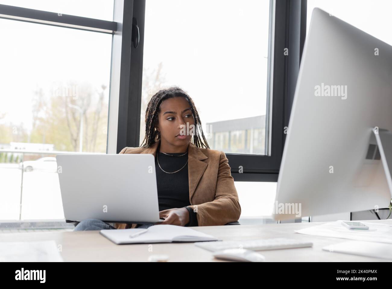 African american businesswoman in jacket holding laptop near computer ...