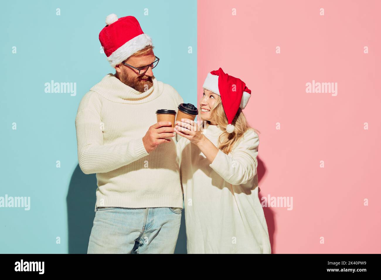 Greetings. Young charming couple wearing christmas hats and white warm ...