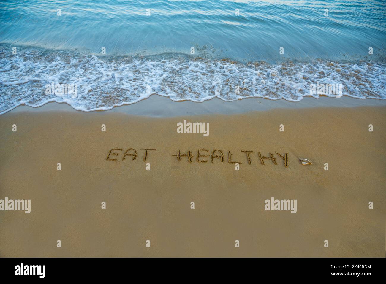 Eat healthy written in the sand on the beach with the sea washing up ...