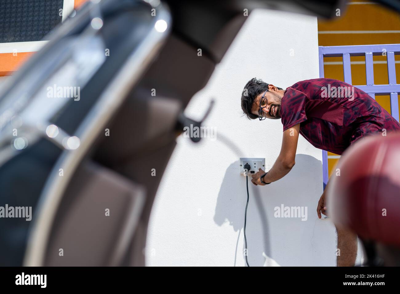 young indain man charging EV or electric scooter battery at charging ...
