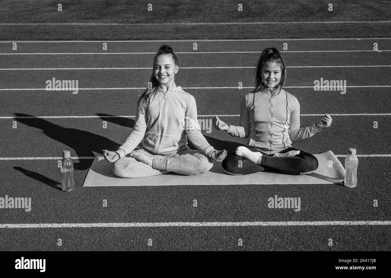 Happy active children meditate sitting in lotus position on yoga mat athletics track, meditation ...