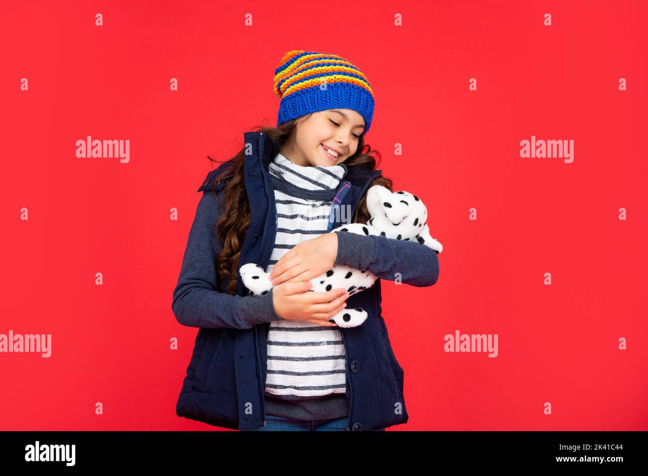 positive child in puffer jacket hold toy. teen girl on red background ...