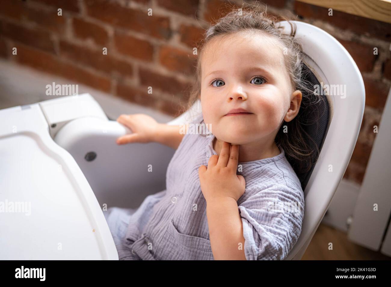 portrait caucasian baby girl about 2 years old in bib eating pasta from plate sitting high chair ...