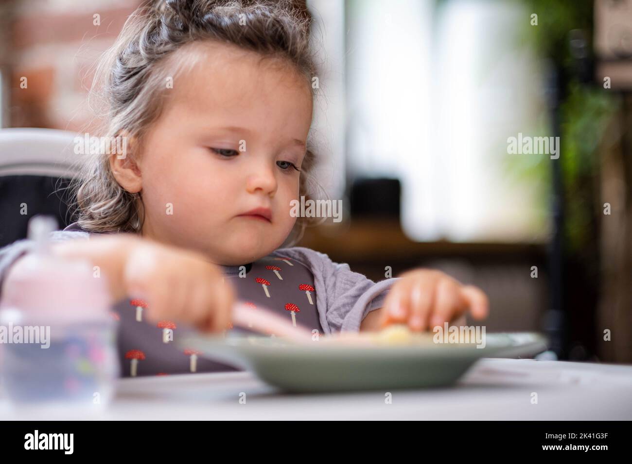 portrait caucasian baby girl about 2 years old in bib eating pasta from ...