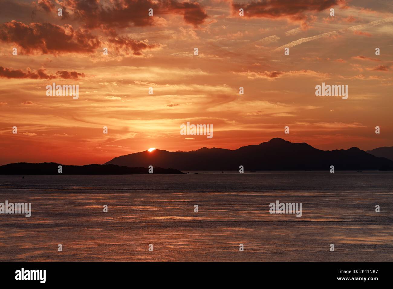 Offshore view of sun setting behind mountains as sky glows orange Stock ...