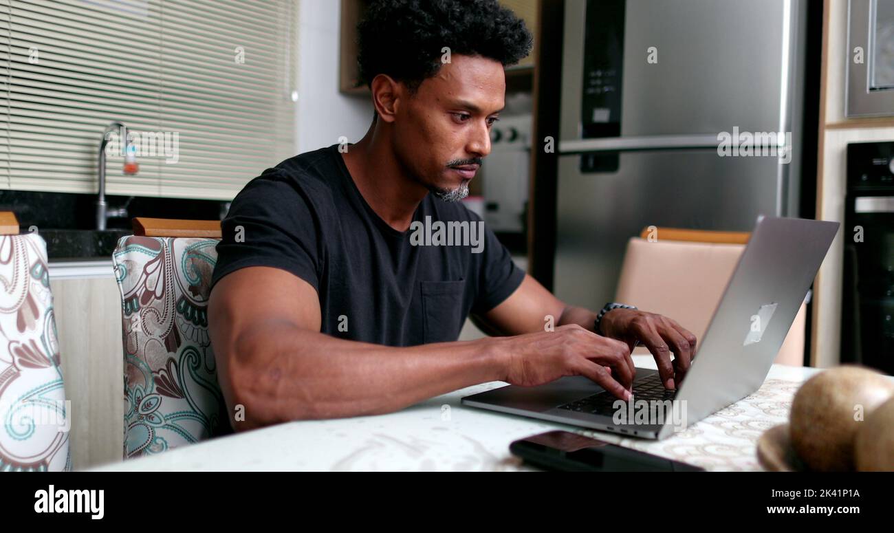 African man working from home sitting at kitchen table using laptop ...