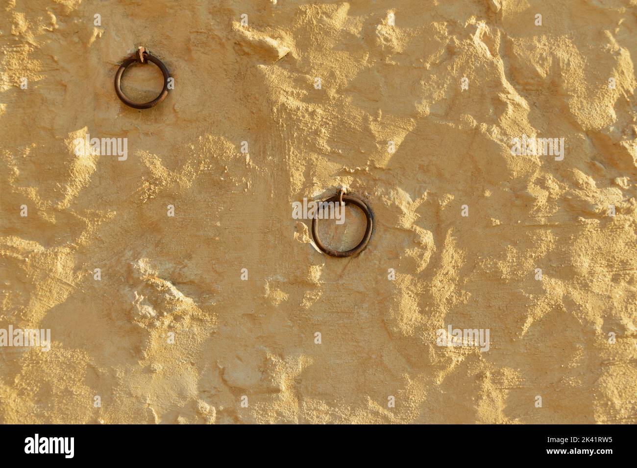 Cement wall with yellow plaster and two iron rings Stock Photo - Alamy