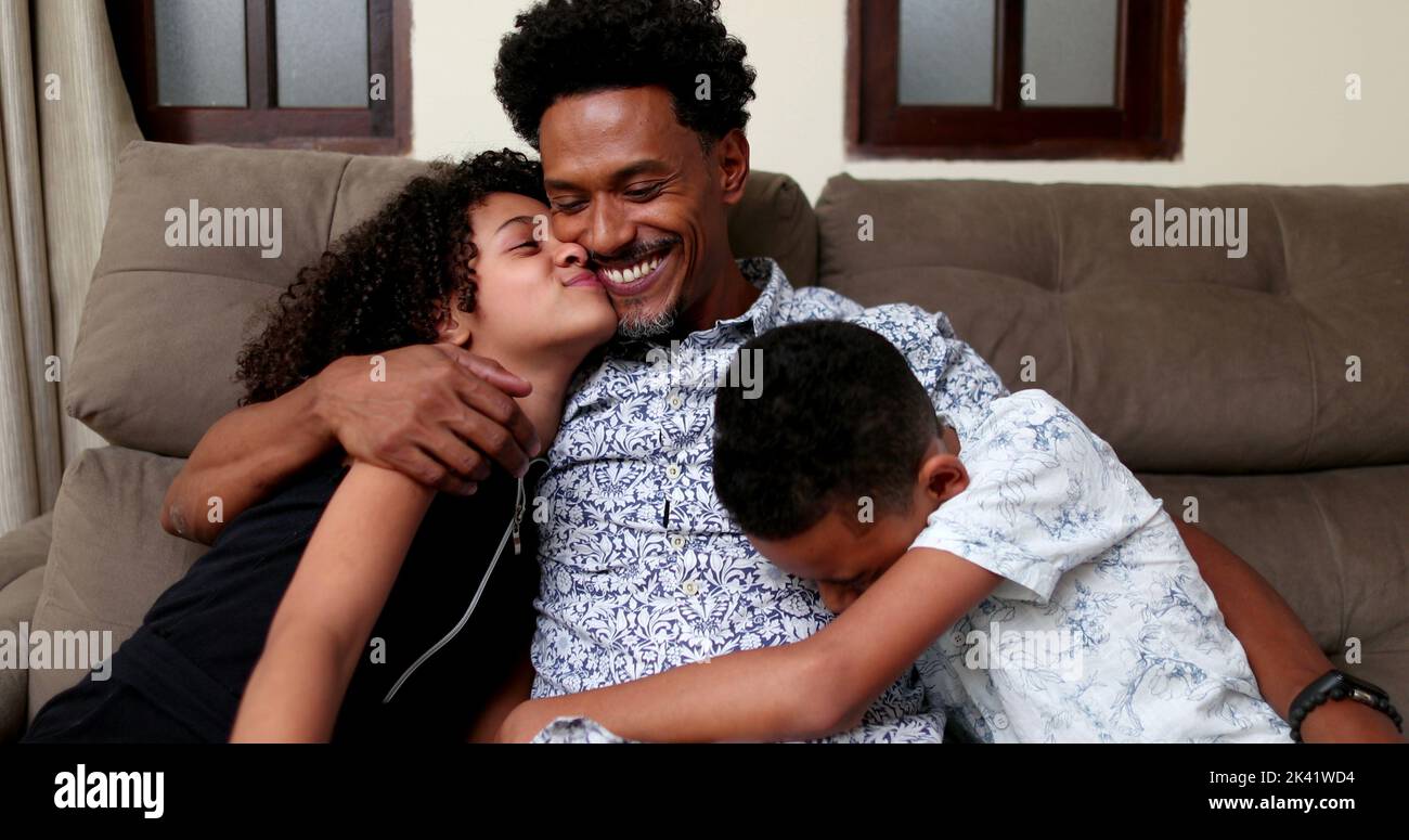 African father embracing daughter and son together at couch living-room ...