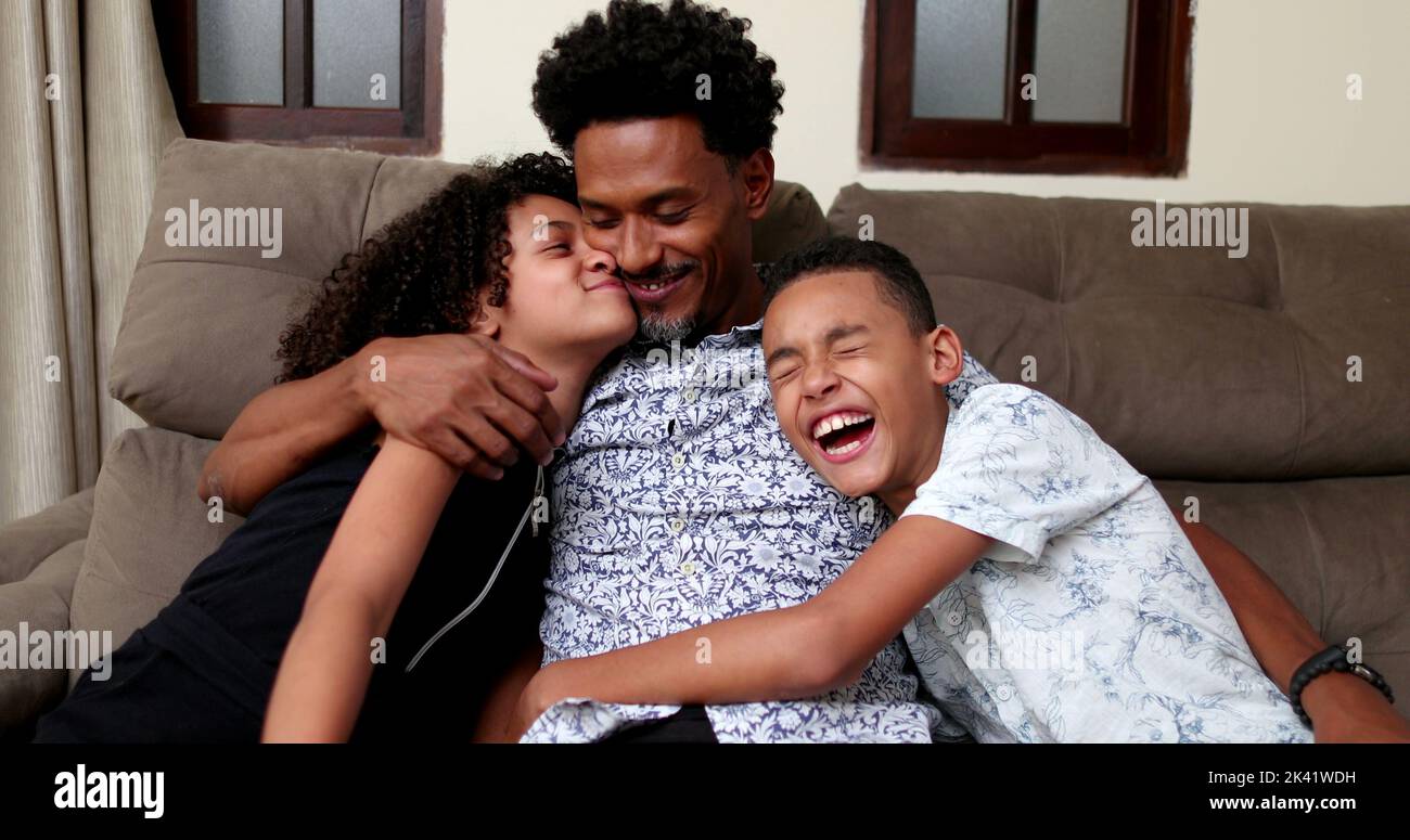 African father embracing daughter and son together at couch living-room ...