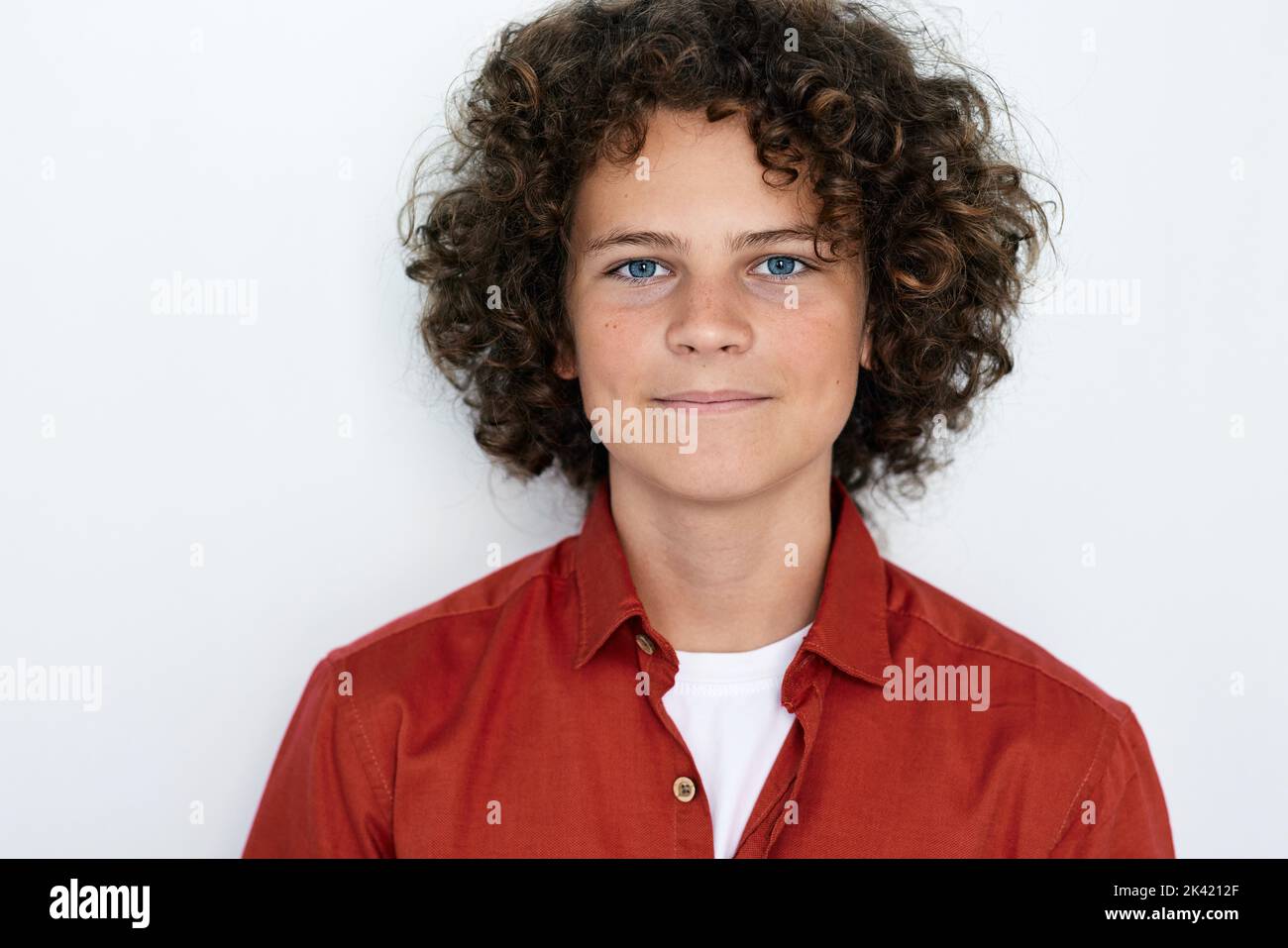 Nice curly boy with blue eyes in red shirt looking at camera, studio ...