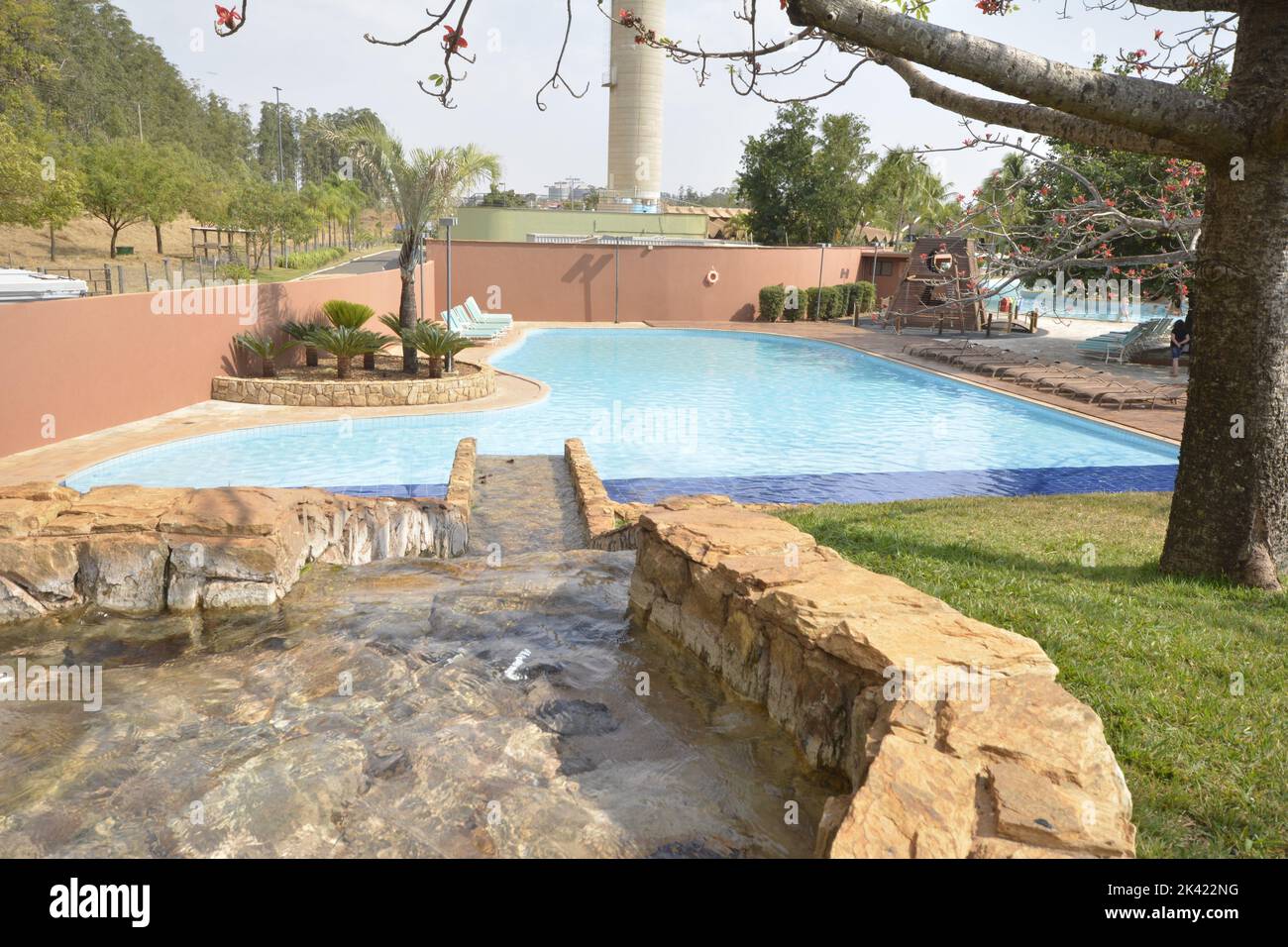 Luxury resort pool with waterfall and sun loungers on a clear blue sky ...