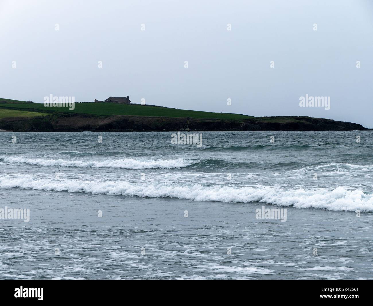 Sea at high tide. A building on a hill. Gray sky, building on green ...