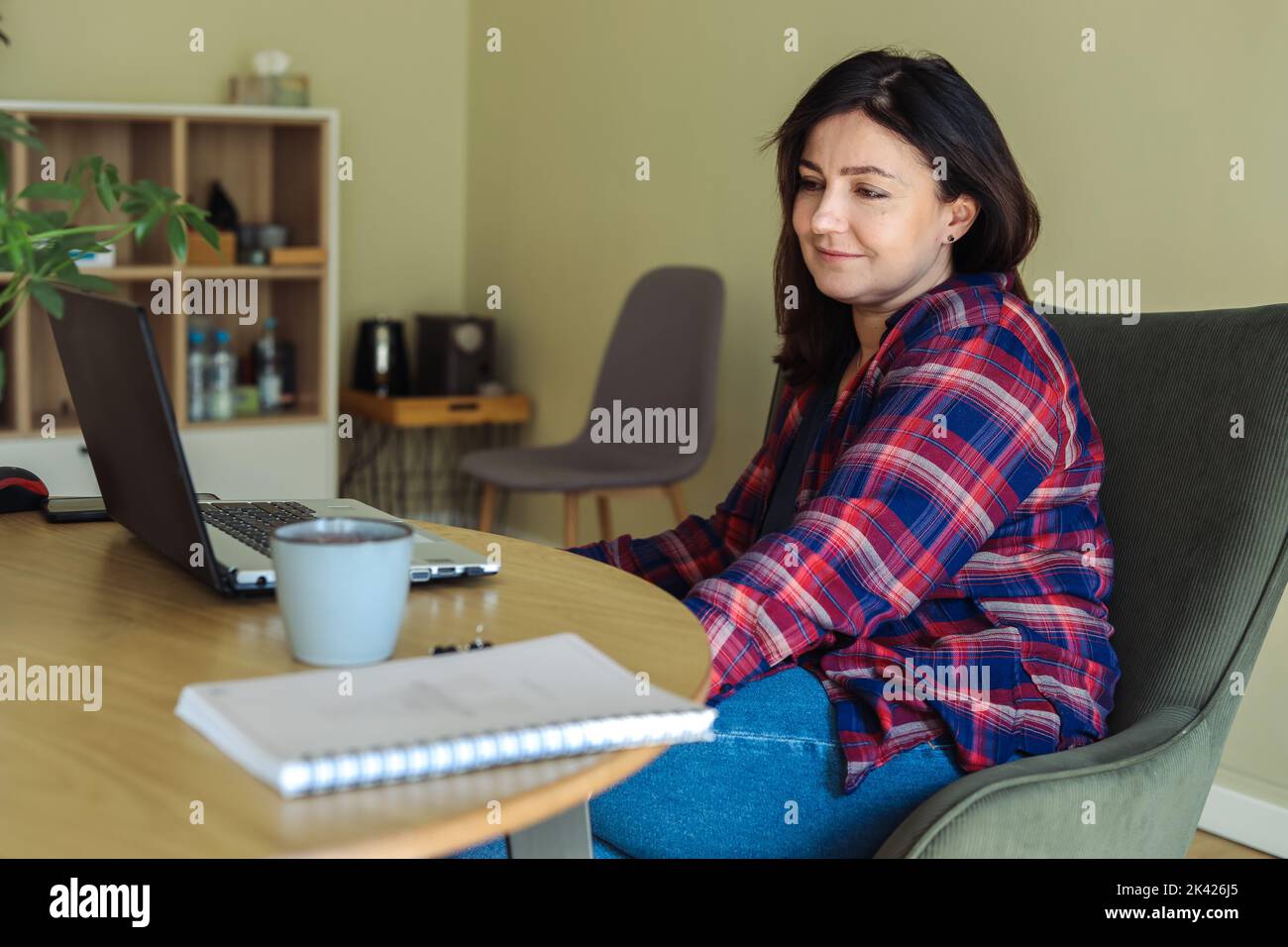 Calm, confident brown-haired woman in plaid shirt working on laptop on ...