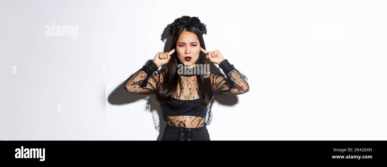 Annoyed and mad asian woman in witch halloween costume shut ears and ...