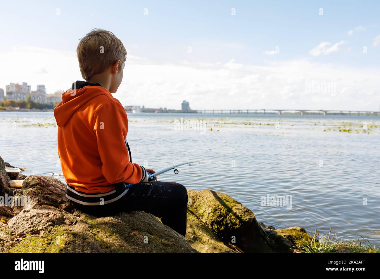 the boy sitting on the stones threw a fishing rod into the river and ...