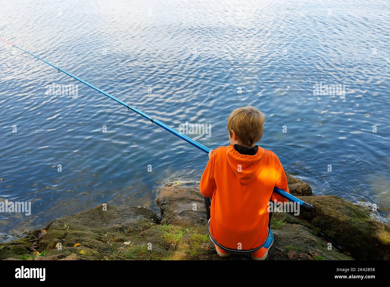 the boy sits with his back and catches fish with a fishing rod in the ...