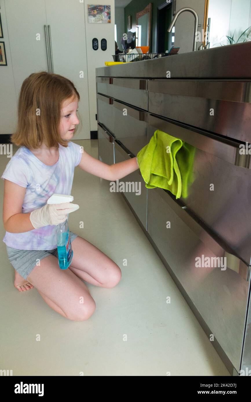 Young girl aged eight years old cleaning and polishing the kitchen with ...
