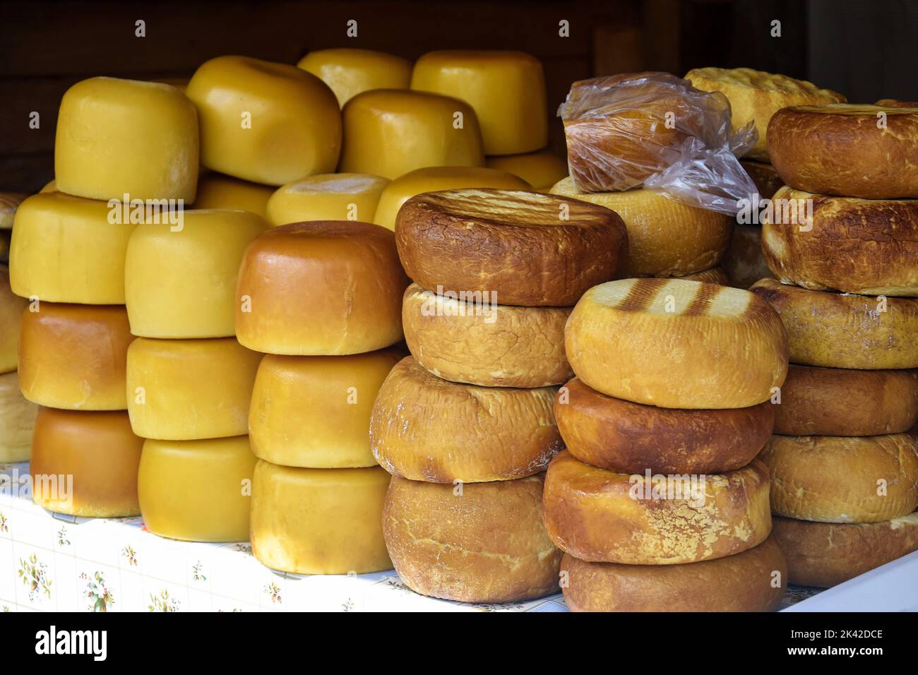Cheese heads of different colors and sizes are stacked on counter. Fair ...