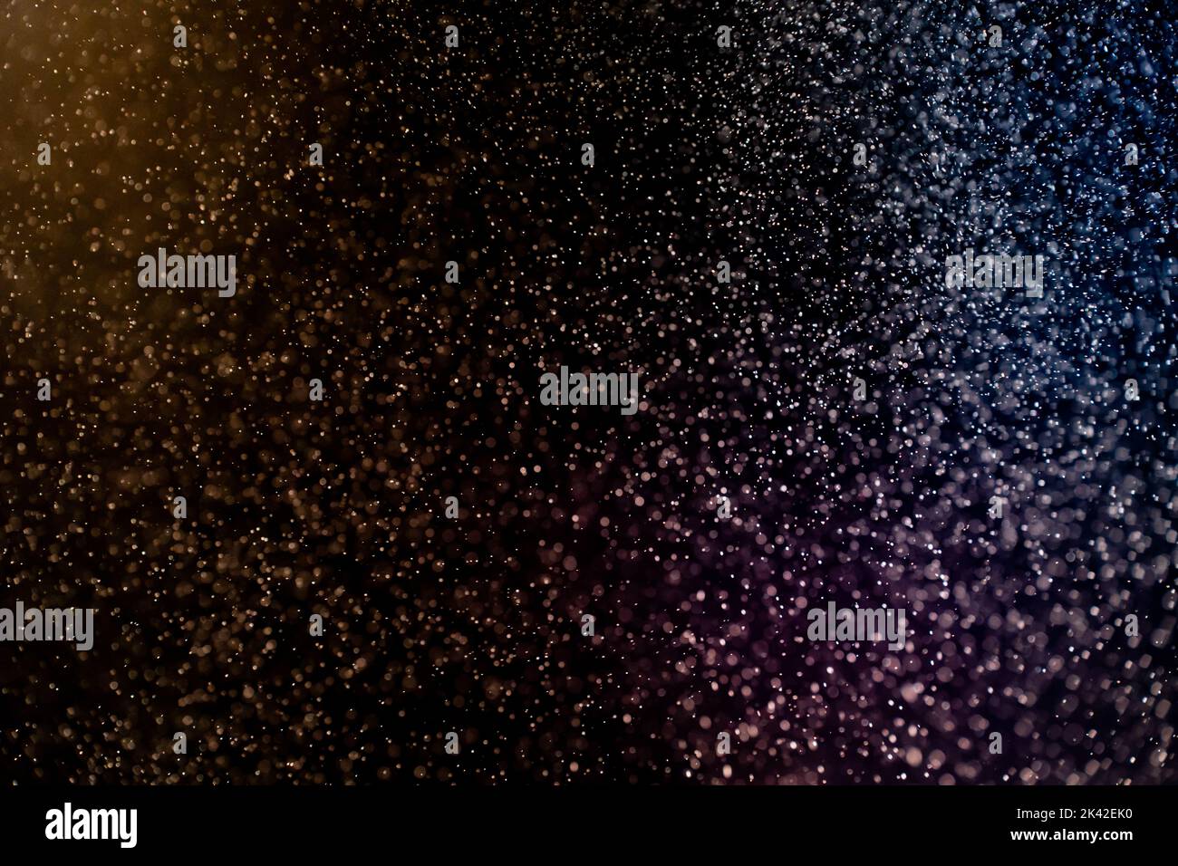 Dust particles floating on a colorful rainbow light on black background ...