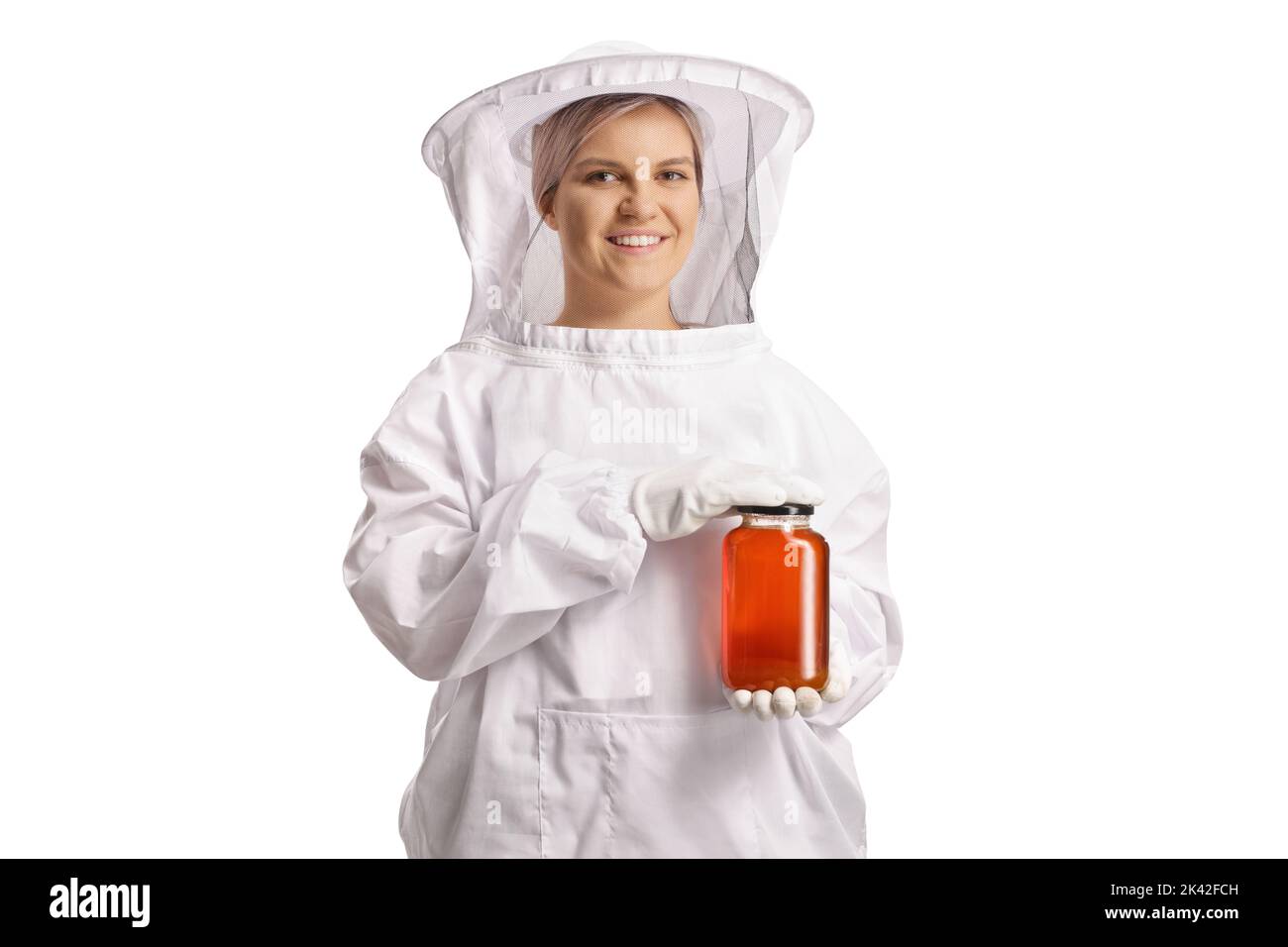 Young female bee keeper in a uniform holding a jar of honey and smiling ...