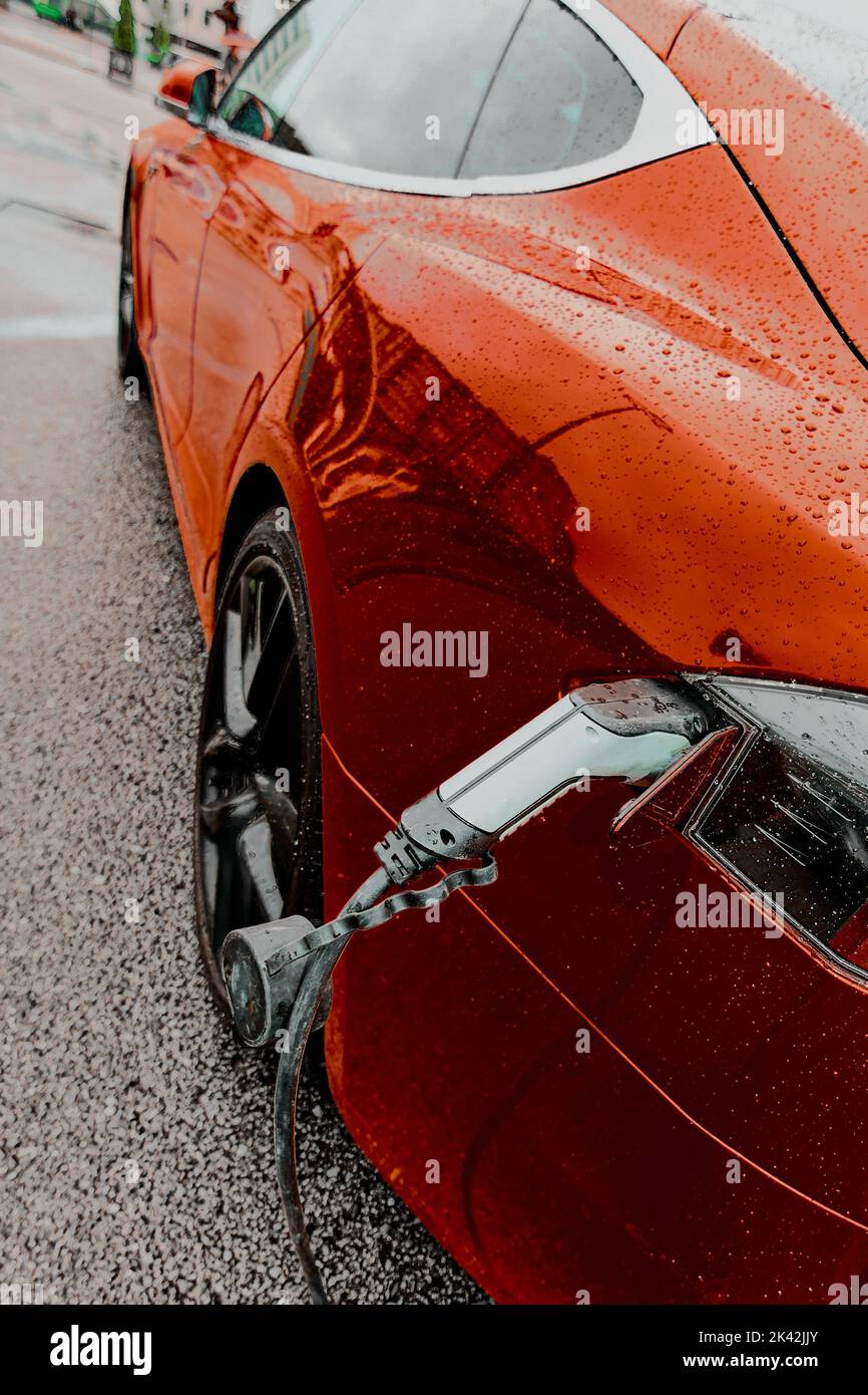 Red electric car on a rainy day connected with an adapter to an to an ...