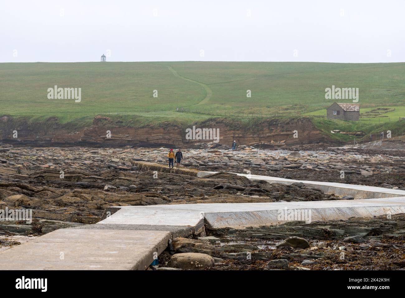 Tourists walking along the concrete pathway to the island Brough of ...