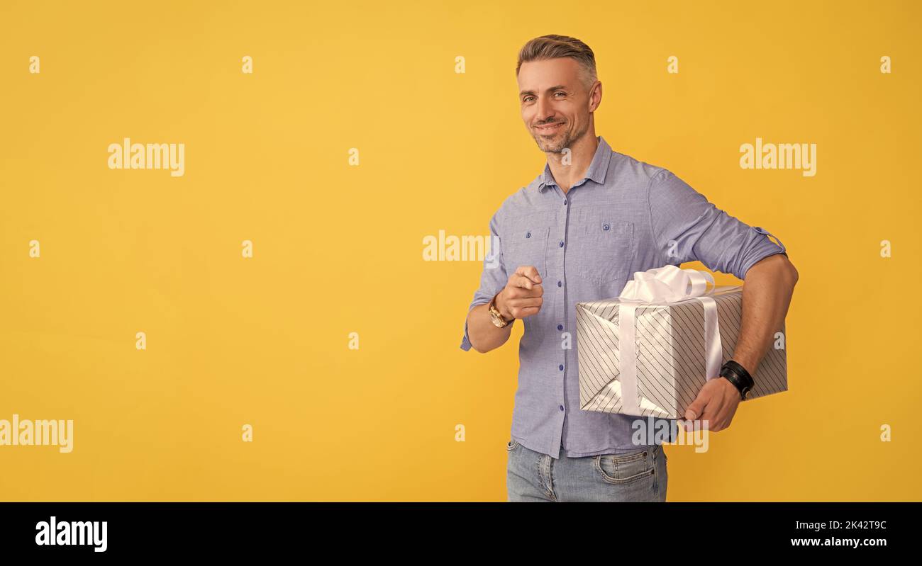 happy mature man hold box pointing finger on yellow background, copy ...