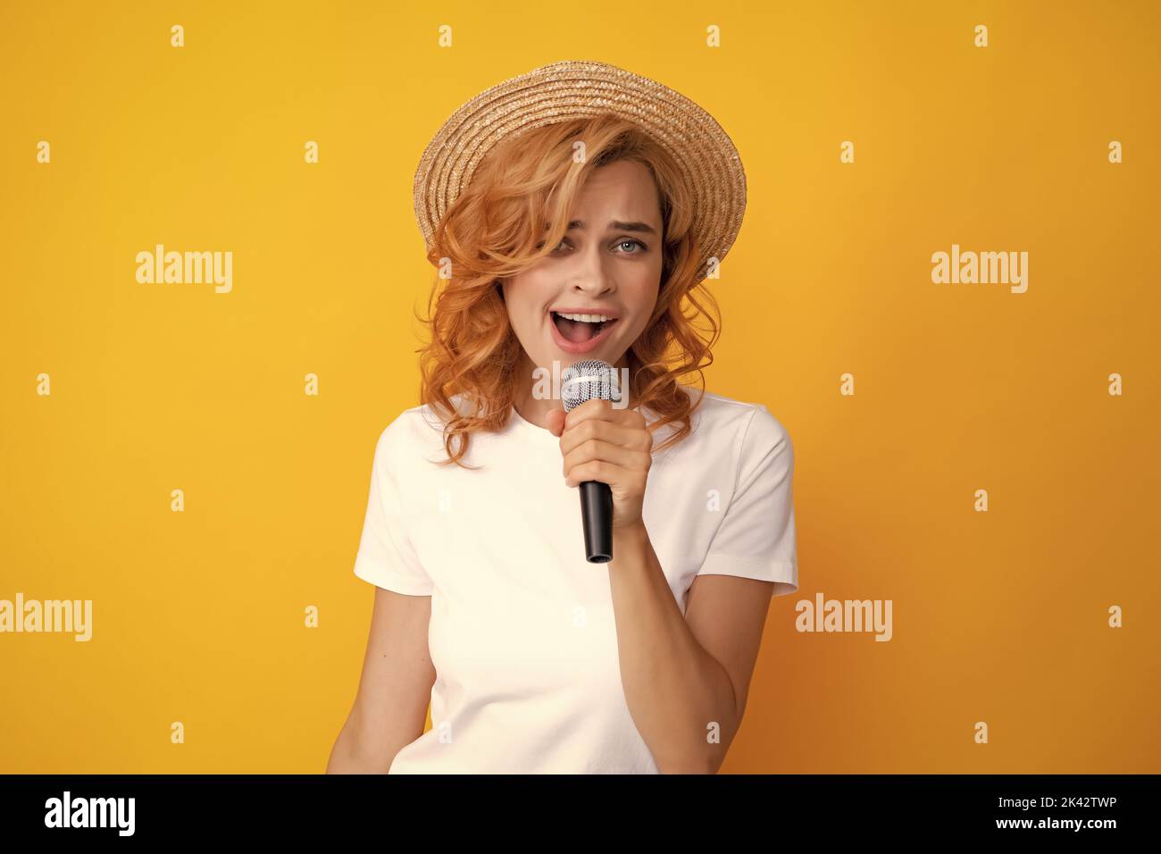 Beautiful young woman singing karaoke isolated on yellow. Girl singing soundtrack song at mic ...