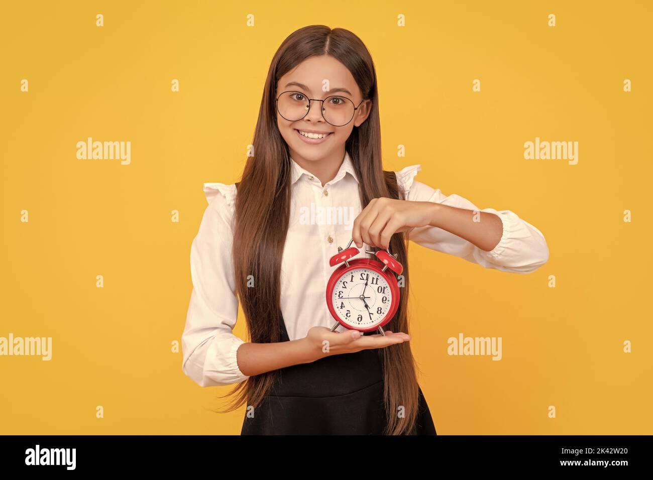 cheerful teen girl in school uniform and glasses with alarm clock ...