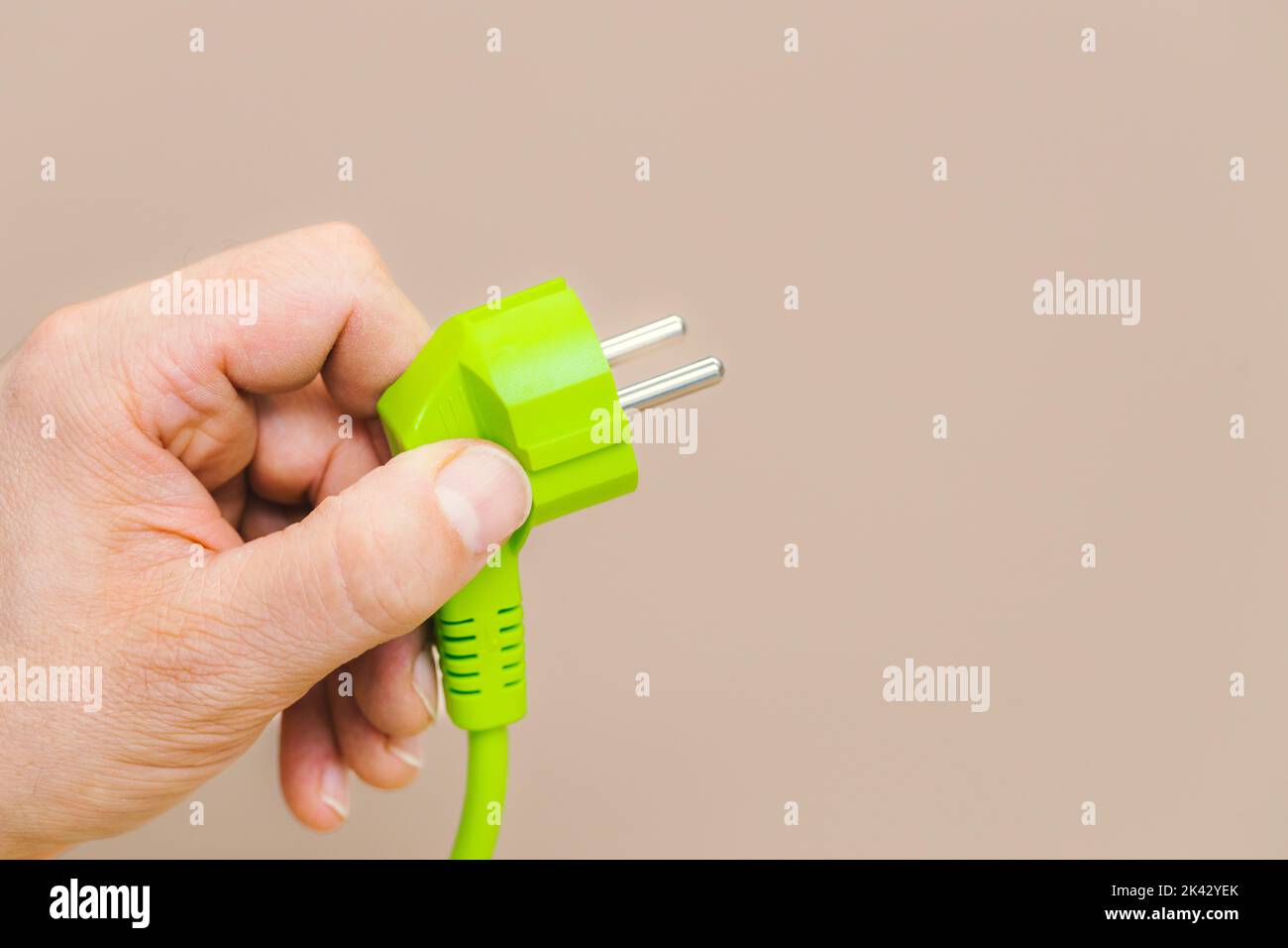 Green plug in hand, Latte-colored background, The concept of using ...