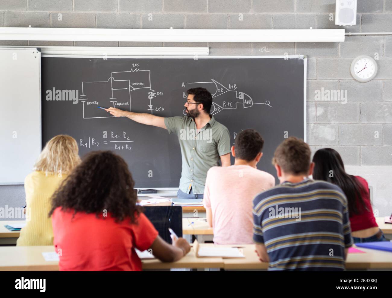 Young male teacher giving a science class explaining at the blackboard ...
