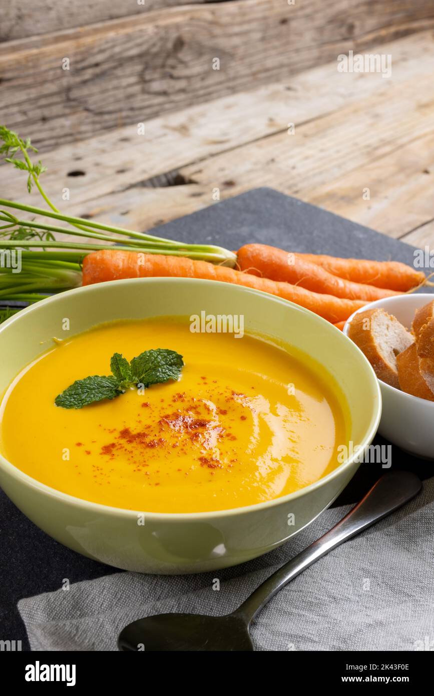 Vertical image of bowl of carrot soup with garnish, carrots and sliced ...