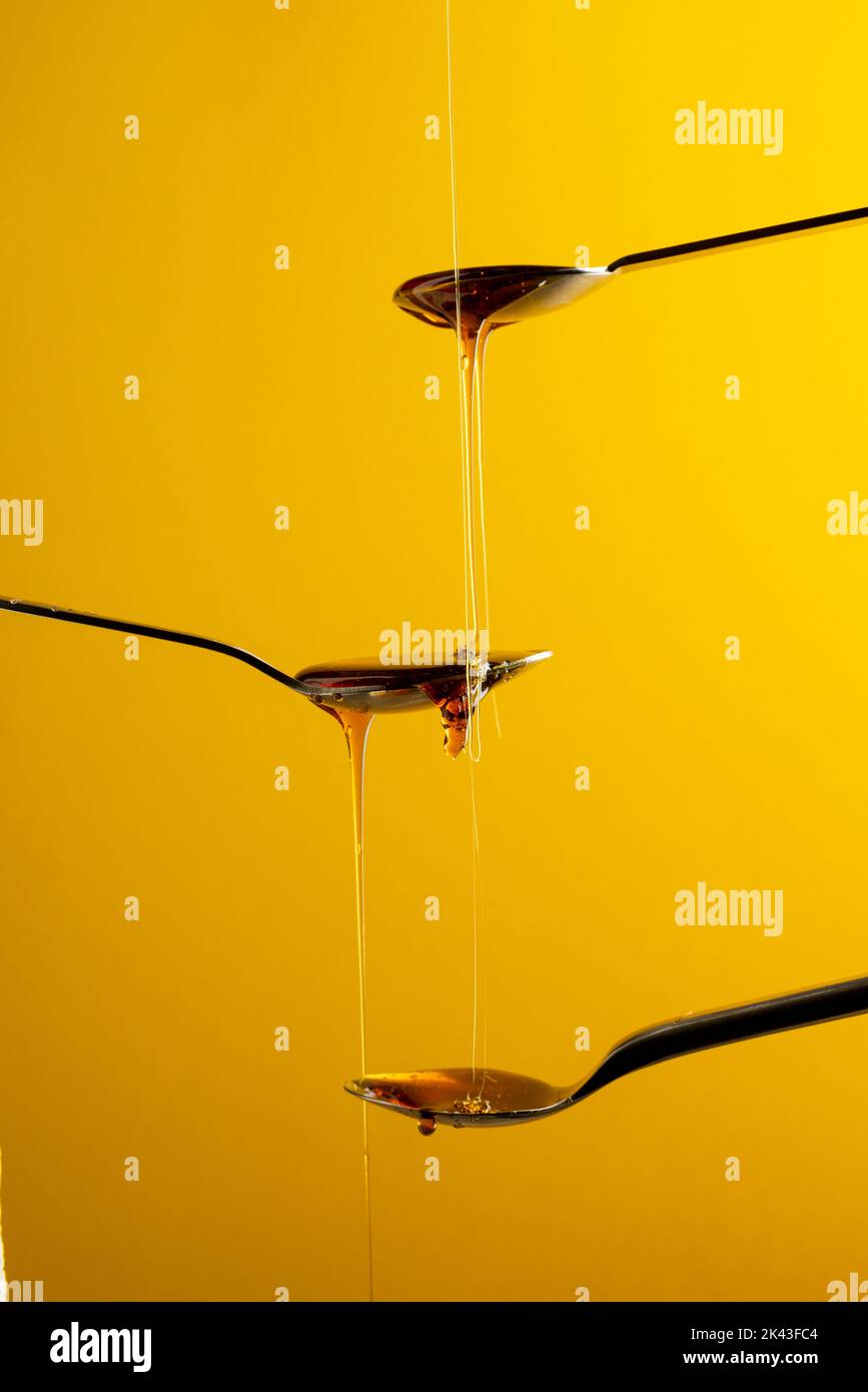 Vertical image of maple syrup dripping between three spoons, on yellow ...