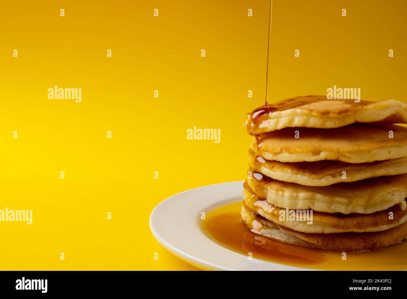 Horizontal image of maple syrup pouring onto stack of pancakes, yellow ...