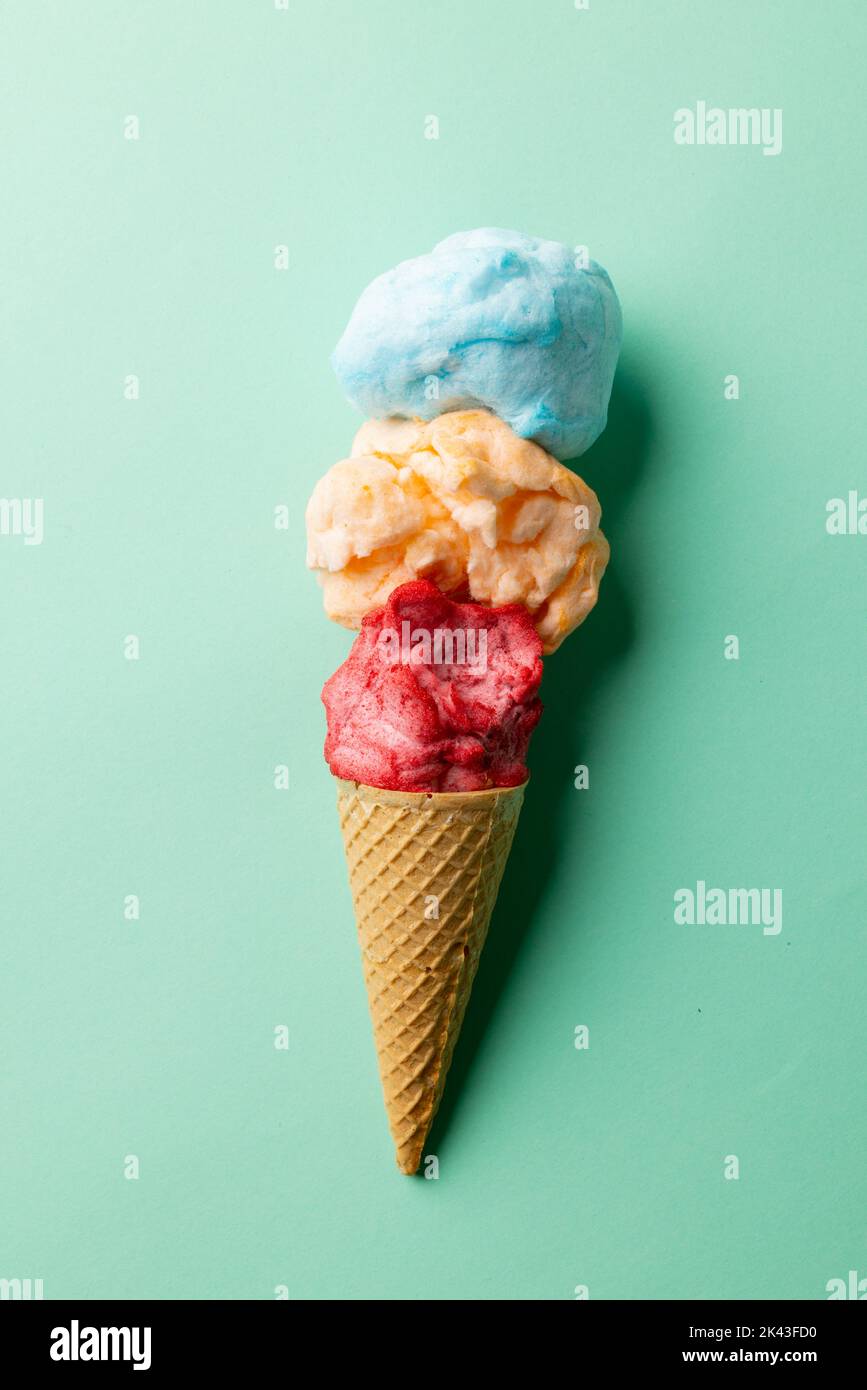 Vertical image of three coloured flavours of ice cream in cone, on blue ...